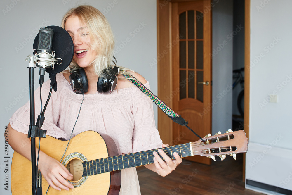Beautiful blonde singer girl in headphones with a guitar in home ...