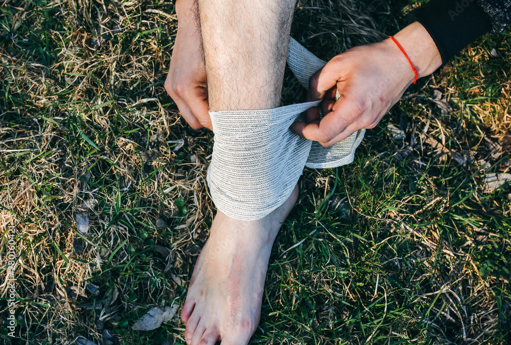 Man is putting bandage on sprained ankle. Twisted leg. Person sitting ...