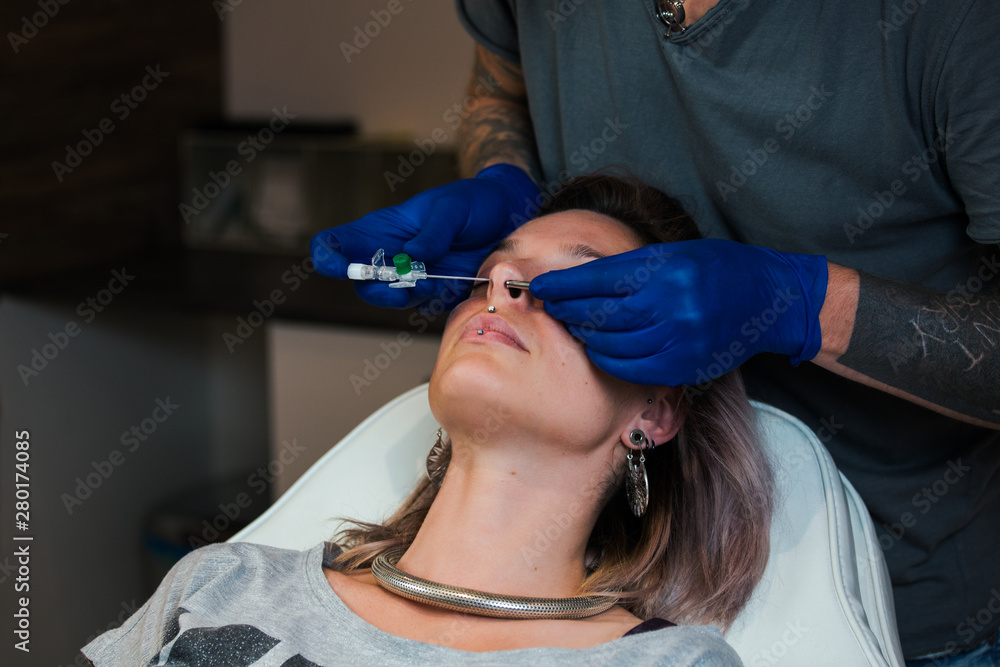 Portrait of a woman getting her nose pierced. Man showing a process of ...