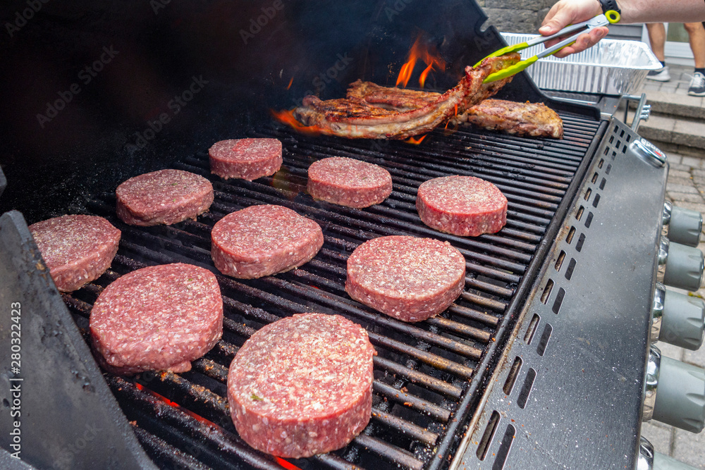 man's hand with tungs over an outdoor Propane gas grill on a deck with ...