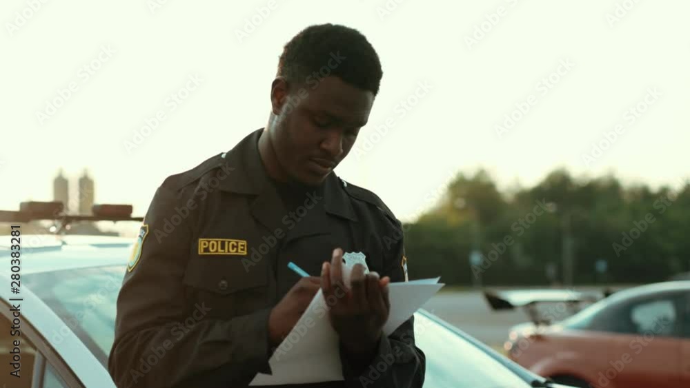 Portrait of young black police officer writing notes at accident ...