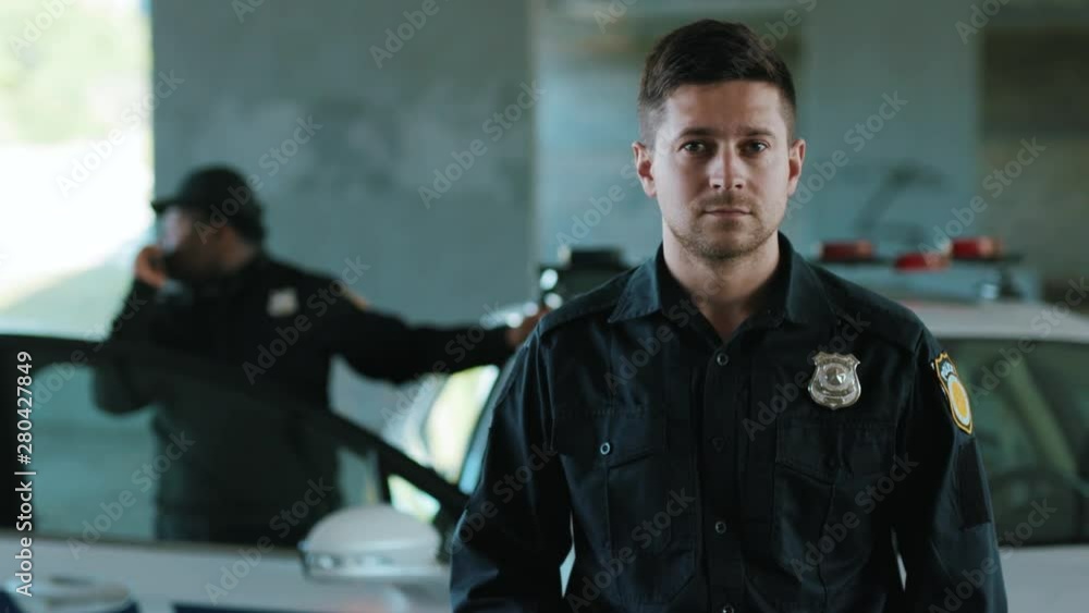 Attractive young man cops stand near patrol car look at camera around ...