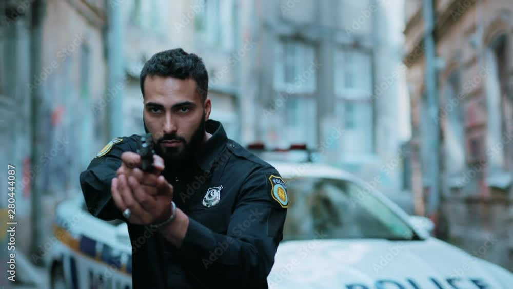 Vidéo Stock Serious young man cops hold pistol stand near patrol car ...