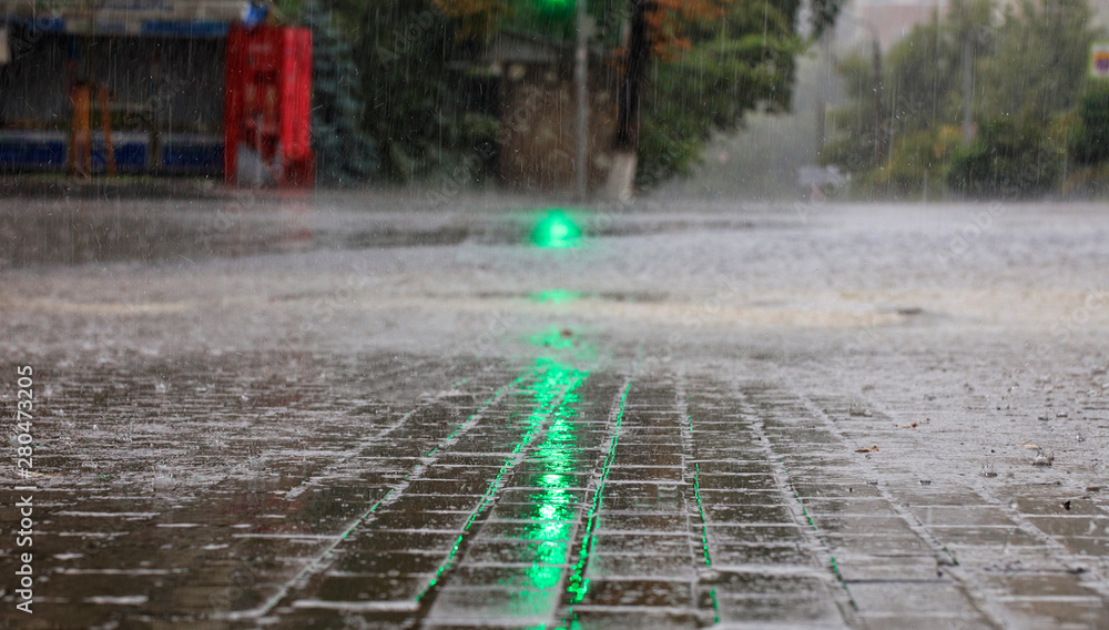 Heavy rain on the sidewalk and asphalt road is illuminated by a green ...