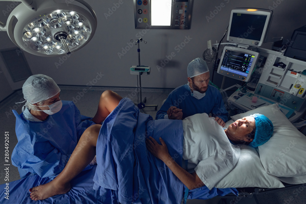 Surgeon examining pregnant woman during delivery while man holding her ...