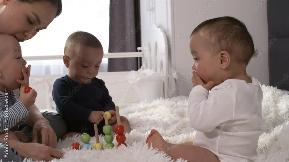Panning shot of Asian baby triplets sitting together with their mom on ...