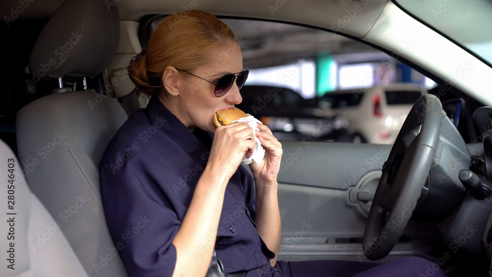 Hungry woman cop eating burger sitting in police car in parking lot ...