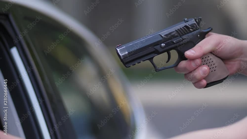 Gun in hands of aggressive mugger screaming and threatening man driving car with firearm through ...