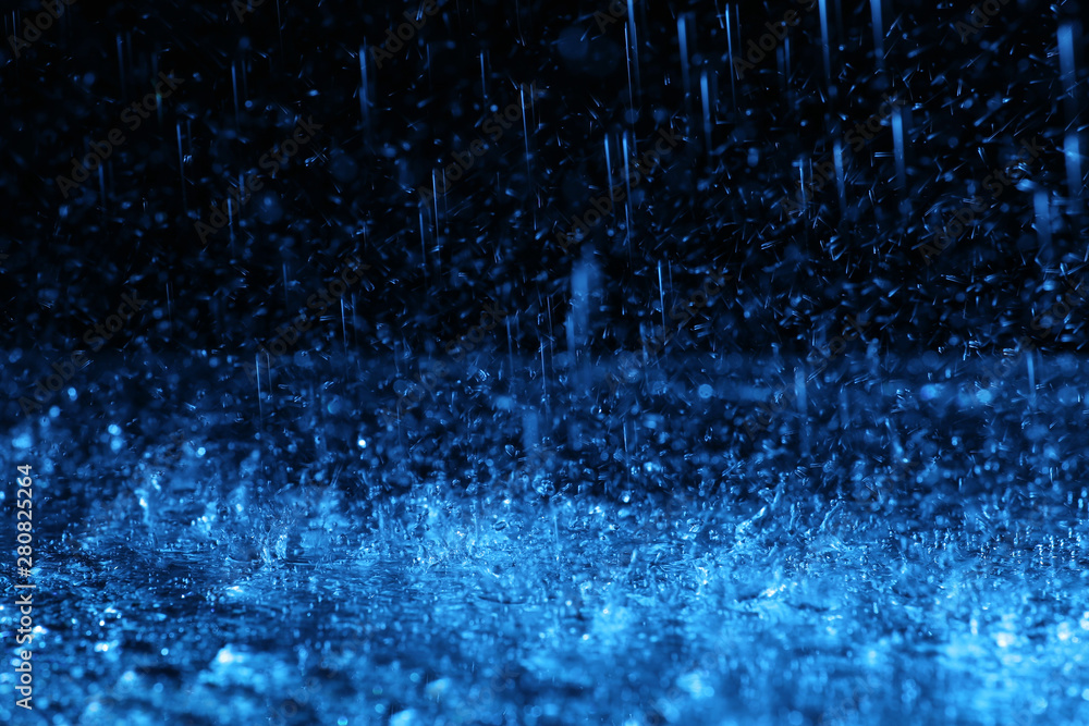 Heavy rain falling down on ground against dark background, toned in ...