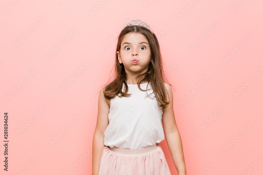 Little girl wearing a princess look blows cheeks, has tired expression ...
