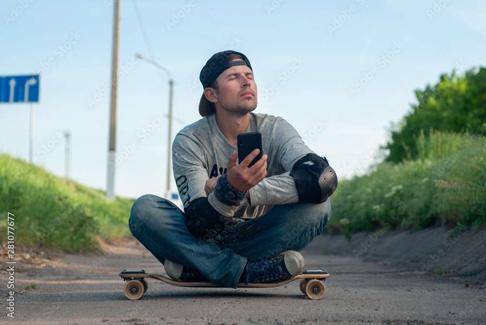Tired happy young skater dozing sitting on a skateboard, breathing ...