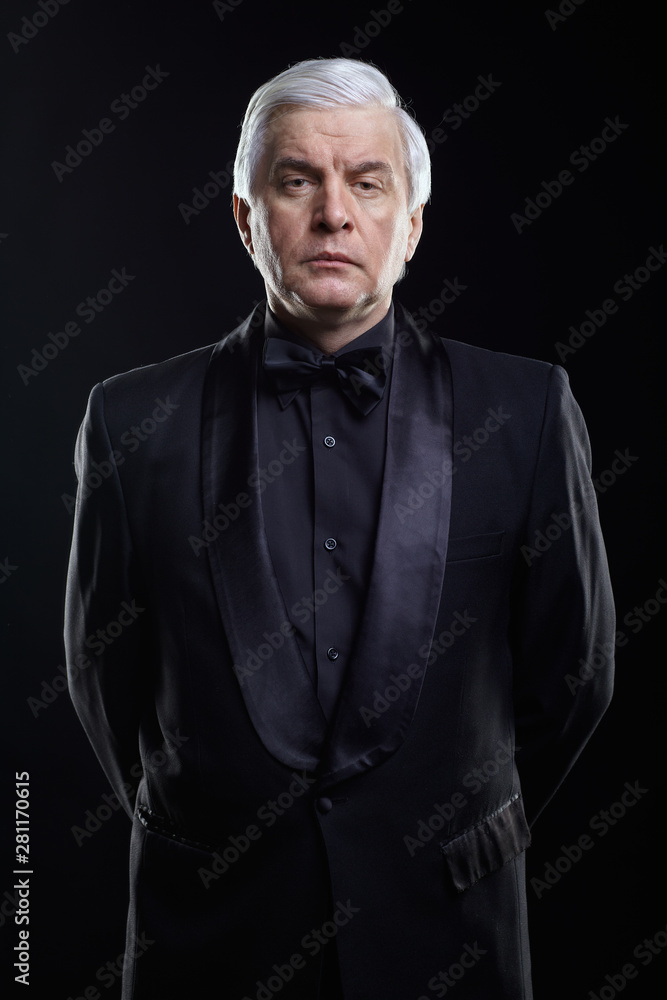 Mature icy calm man in black suit looking at the camera with a hypnotic ...
