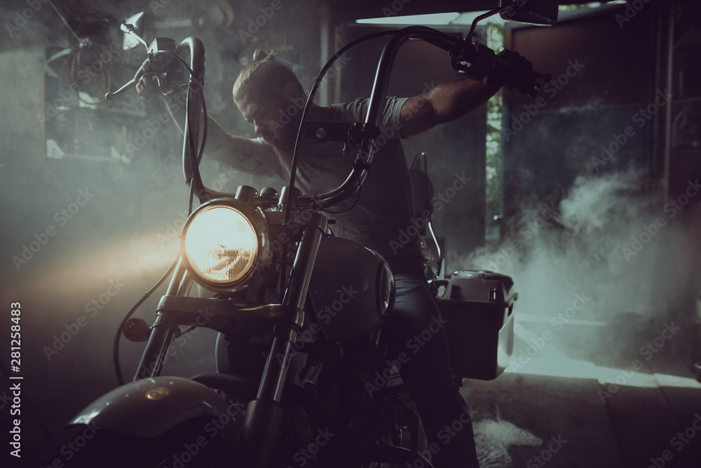 Handsome brutal man with a beard sitting on a motorcycle in his garage ...