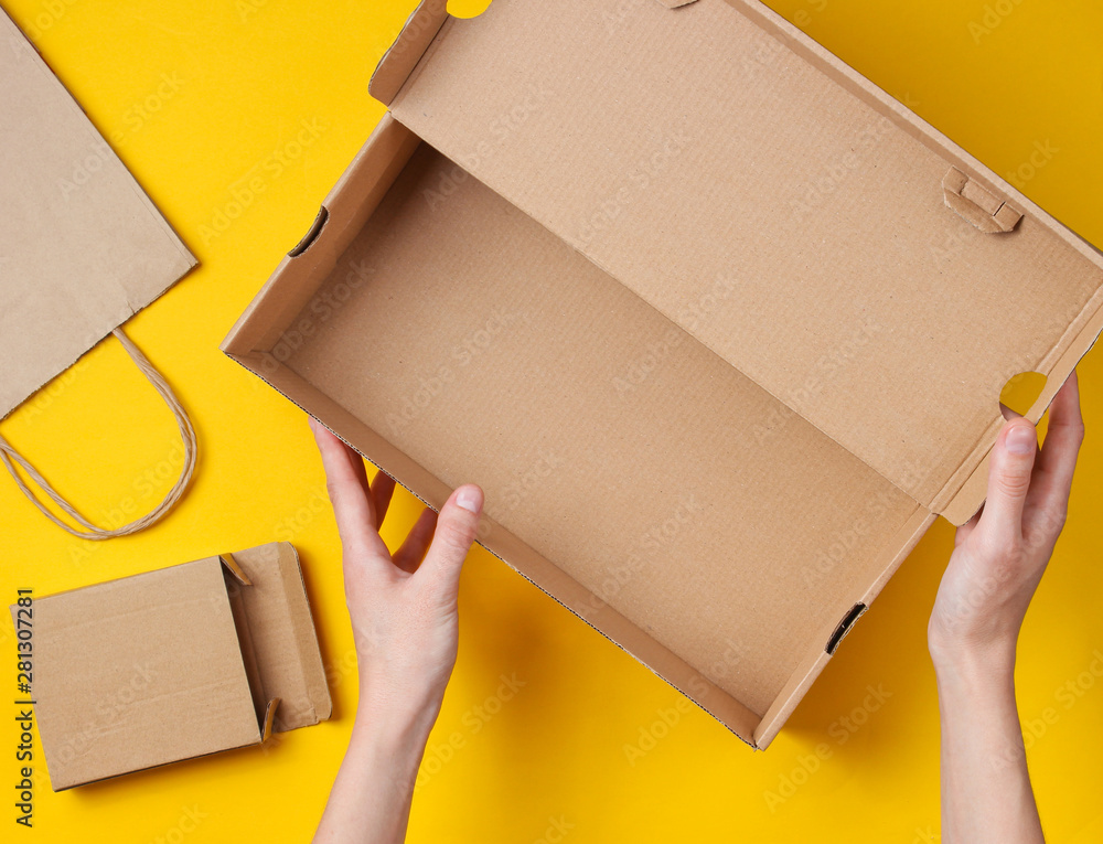Female hands hold an empty cardboard box on a yellow background with a ...