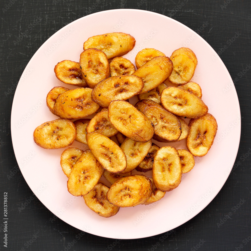 Homemade fried plantains on a pink plate on a black surface, top view ...