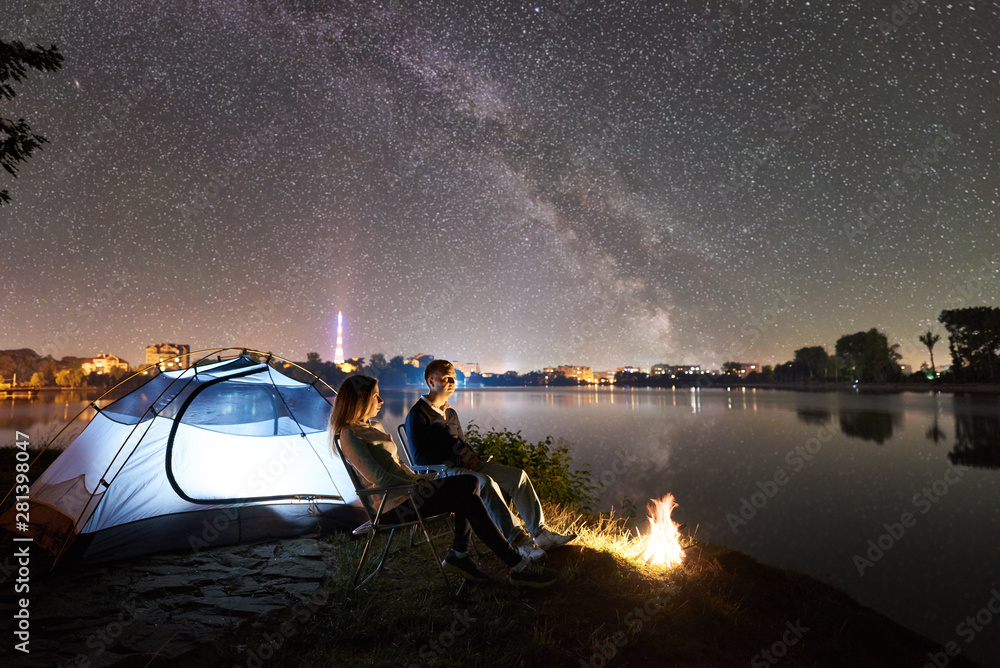 Night camping on lake shore. Couple tourists - man and woman sitting on ...