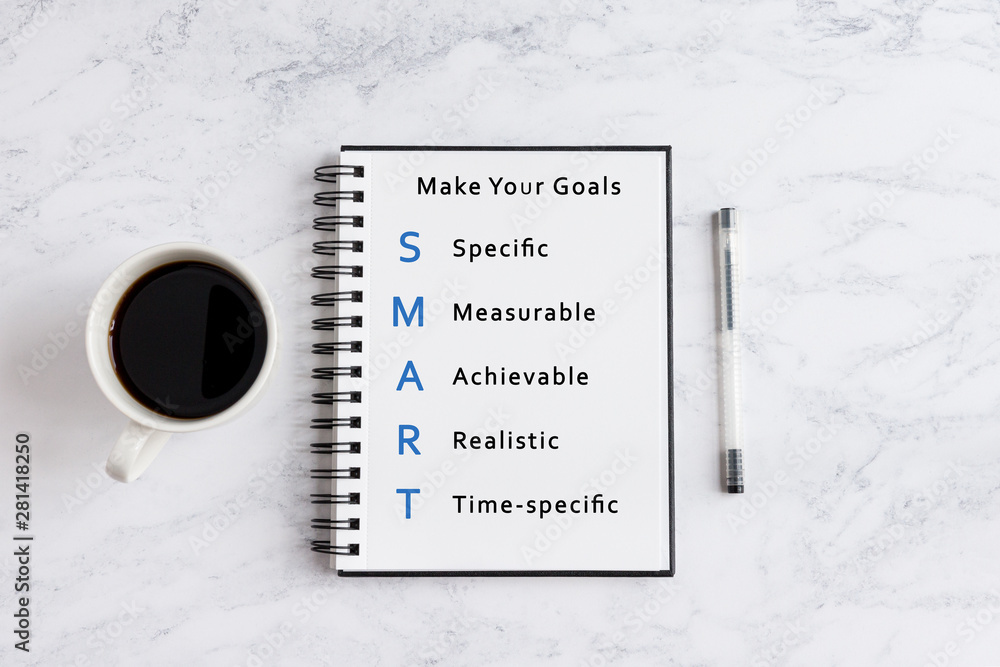 SMART goals writing on notebook. Notebook on desk with coffee cup and a ...