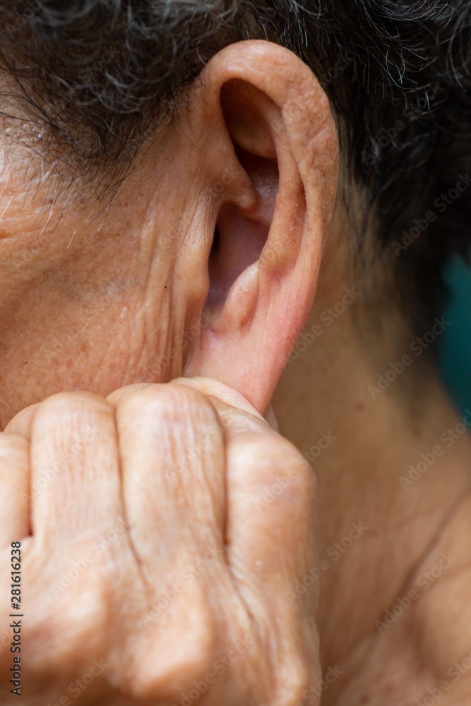 Senior woman's left hand pulling down her left ear, Grey curly hairs ...