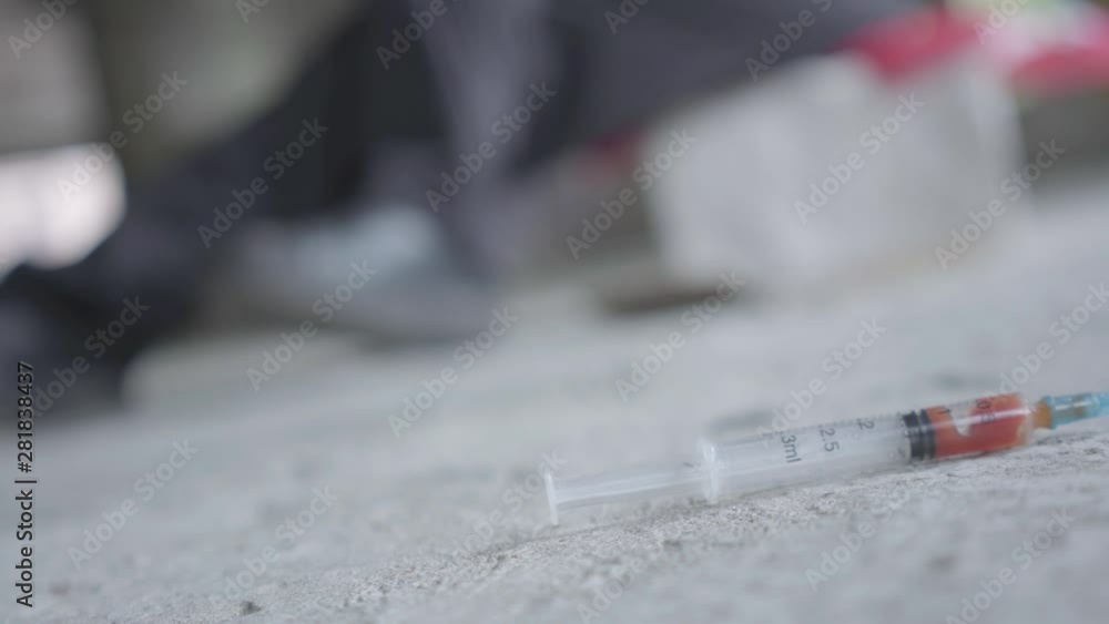 Used syringe with blood inside lying on the concrete floor close up ...