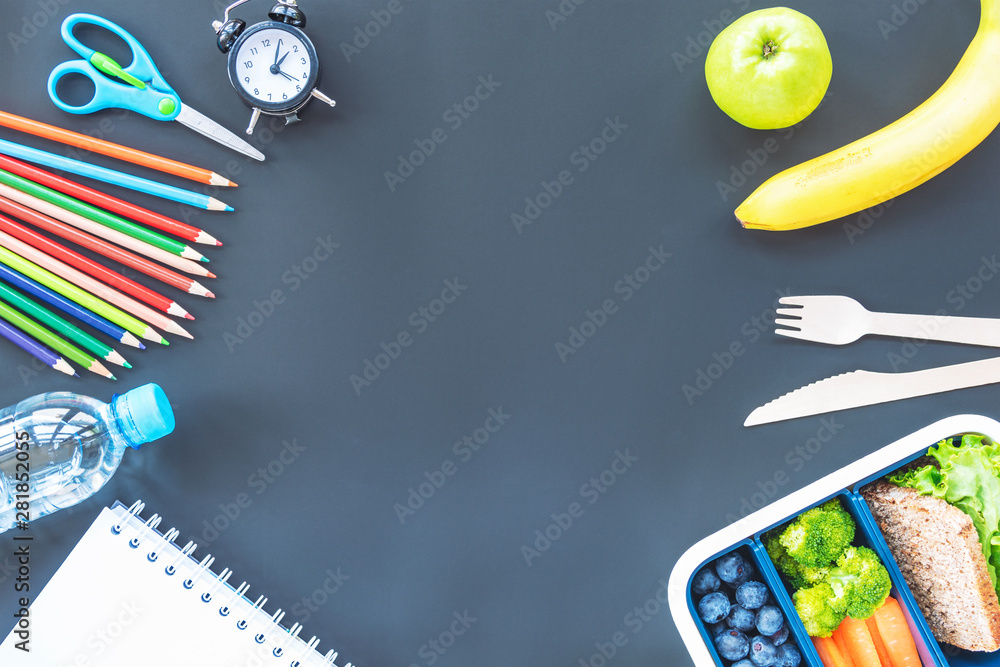 School lunch box with sandwich, vegetables, water and fruits on black ...