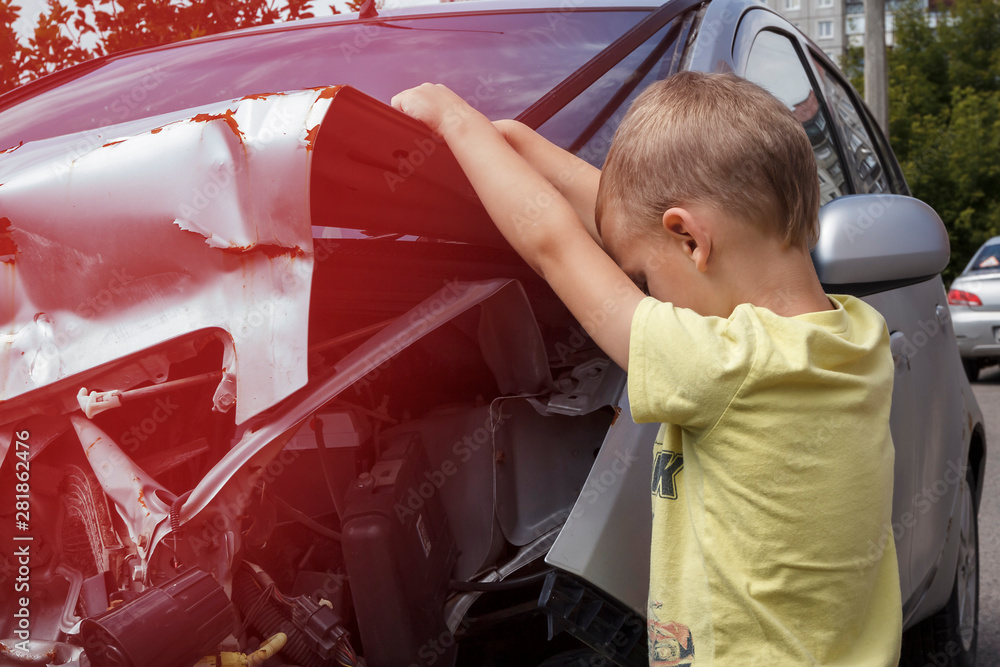 Sad crying baby is standing next to a broken car. Car crash concept ...