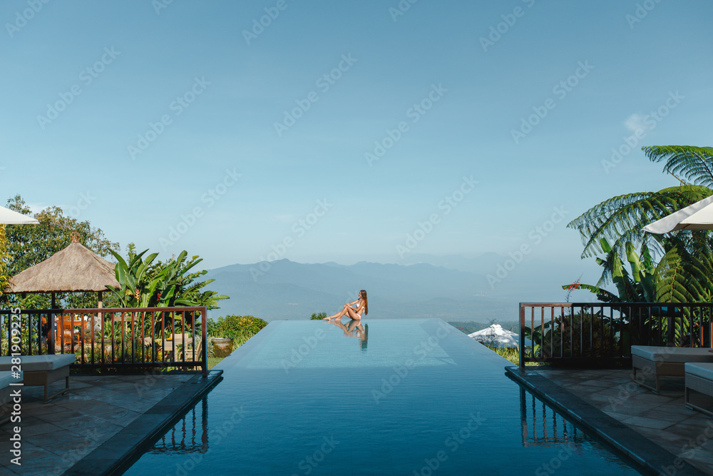 Slim young woman in swimsuit relaxing on edge tropical infinity pool in ...