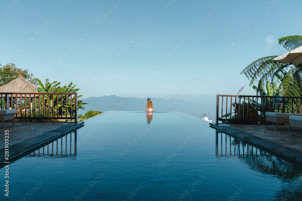 Slim young woman in swimsuit relaxing on edge tropical infinity pool in ...