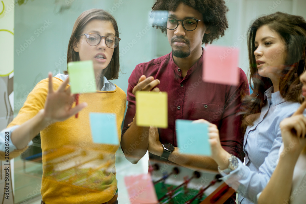 Young business people discussing in front of glass wall using post it ...