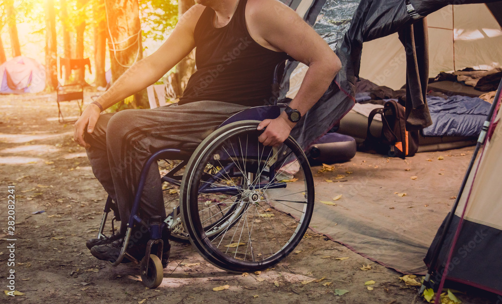 Disabled man resting in a campsite with friends. Wheelchair in the ...
