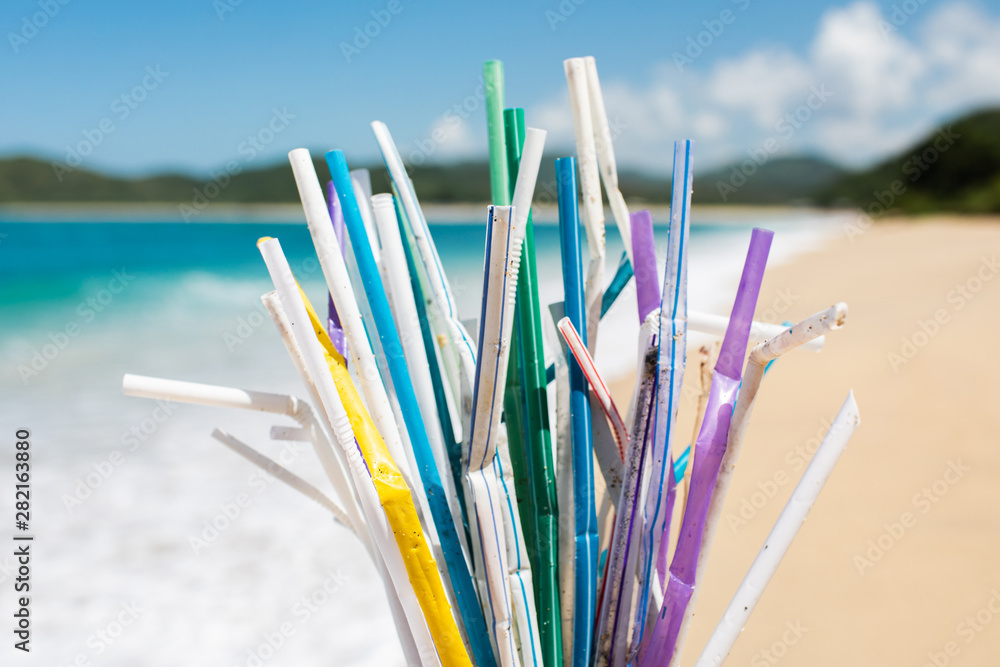 Heap of used plastic straws on background of clean beach and ocean ...