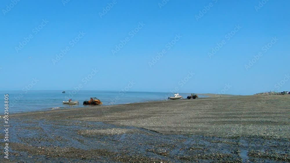 Two tractors on beach; in background a tractor is towing a fishing ...
