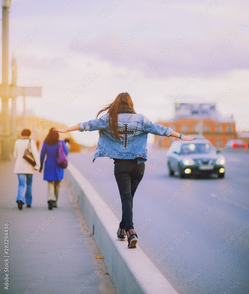 Fearless girl walking on the sidewalk on a busy road, balancing hands ...
