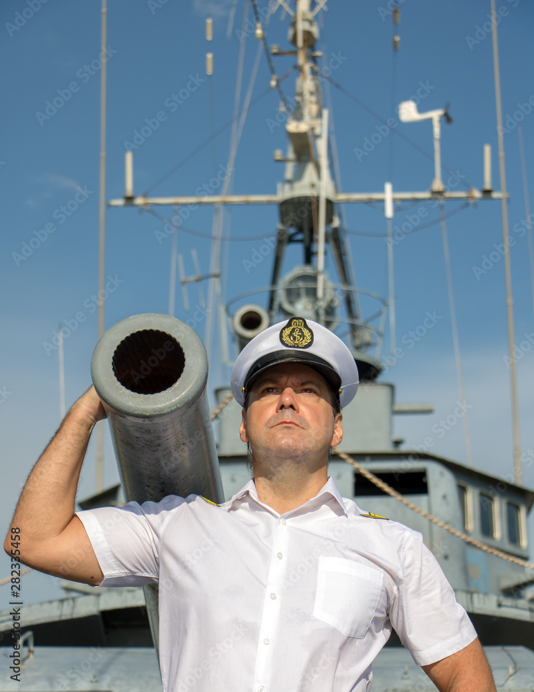 A navy officer standing under a ship's cannon.The captain in white ...