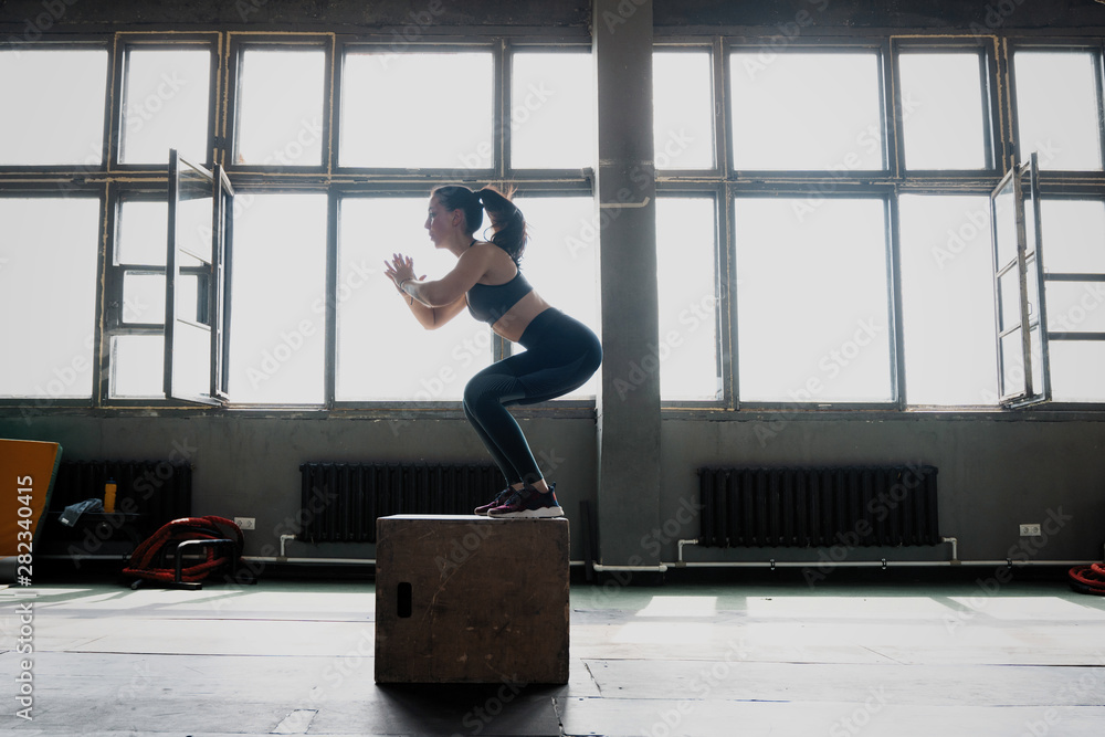 Fit young woman box jumping at a crossfit style gym. Female athlete is ...