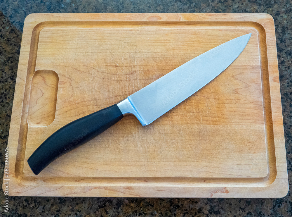 Isolated large chef’s knife on a large wooden cutting board with a ...