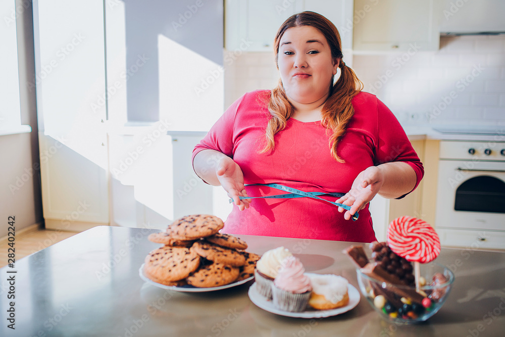 Fat young woman in kitchen sitting and eating sweet food. Soft tape ...
