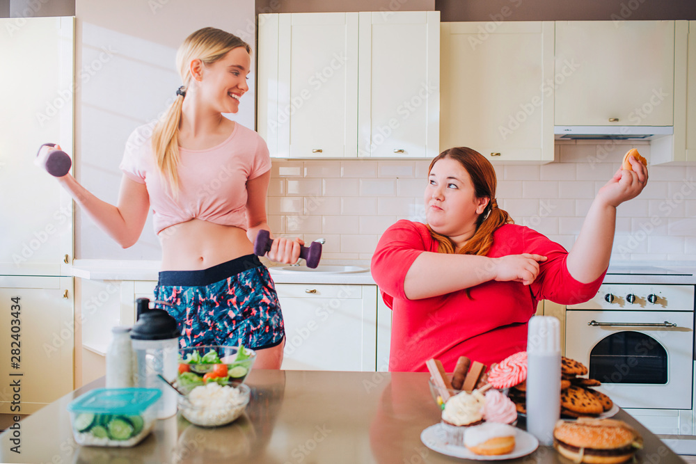 Young sim woman holding dumbbells. Looking at fat plus size model. Body ...