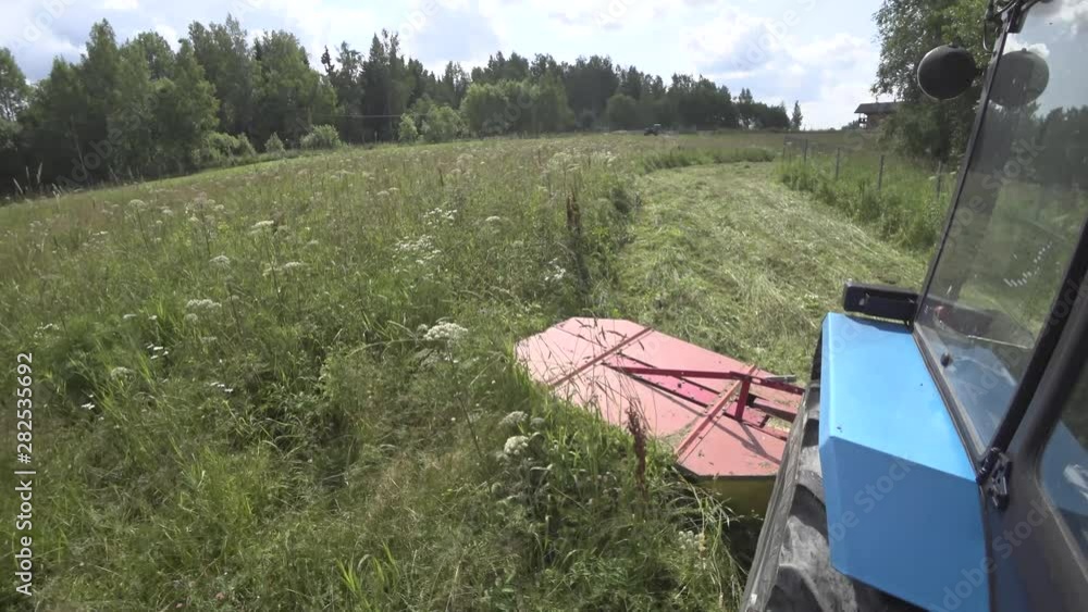 Tractor with rotary mower slowly rides on an inclined field at the end ...