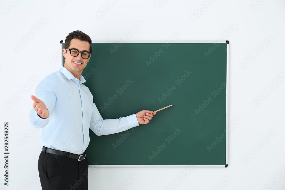 Young teacher with ruler near blank chalkboard in classroom. Space for ...