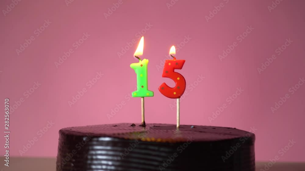 Chocolate birthday cake on pink background with green and red number fifteen candle in middle ...