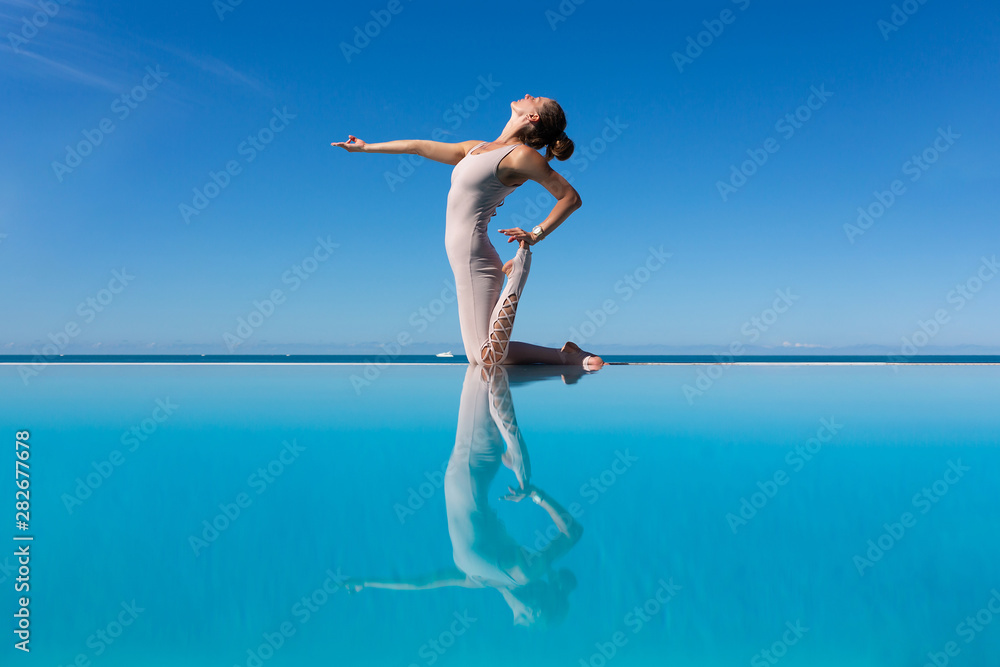 Graceful woman model doing ushtrasana standing on the edge of a pool ...