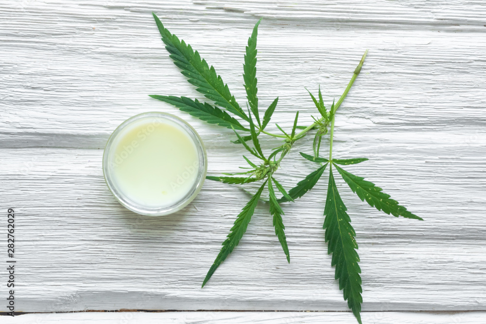 Cannabis cosmetic cream in a jar and a green plant leaf on a white ...