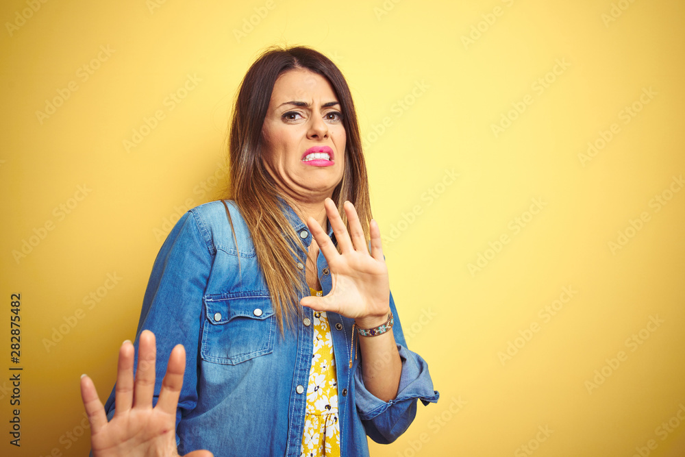 Young beautiful woman standing over yellow isolated background ...