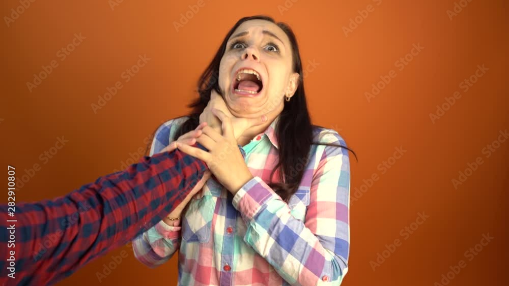 A man's hand in a shirt strangles a scared young woman on an orange ...