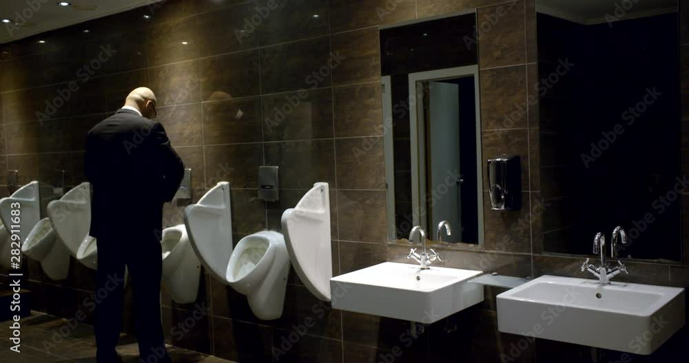 Bald man businessman in suit in between work pees in urinal in public ...