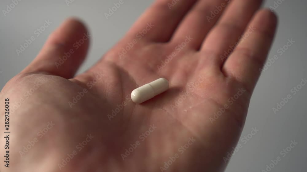 The palm of a hand with a white medical capsule extends. The capsule ...
