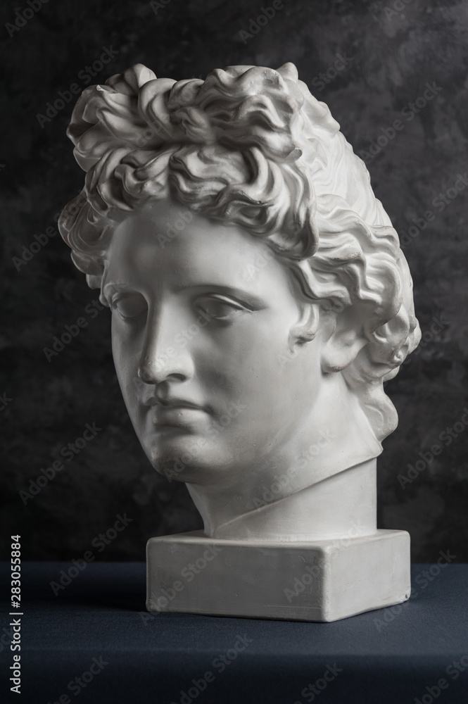 Gypsum copy of ancient statue Apollo head on dark textured background ...