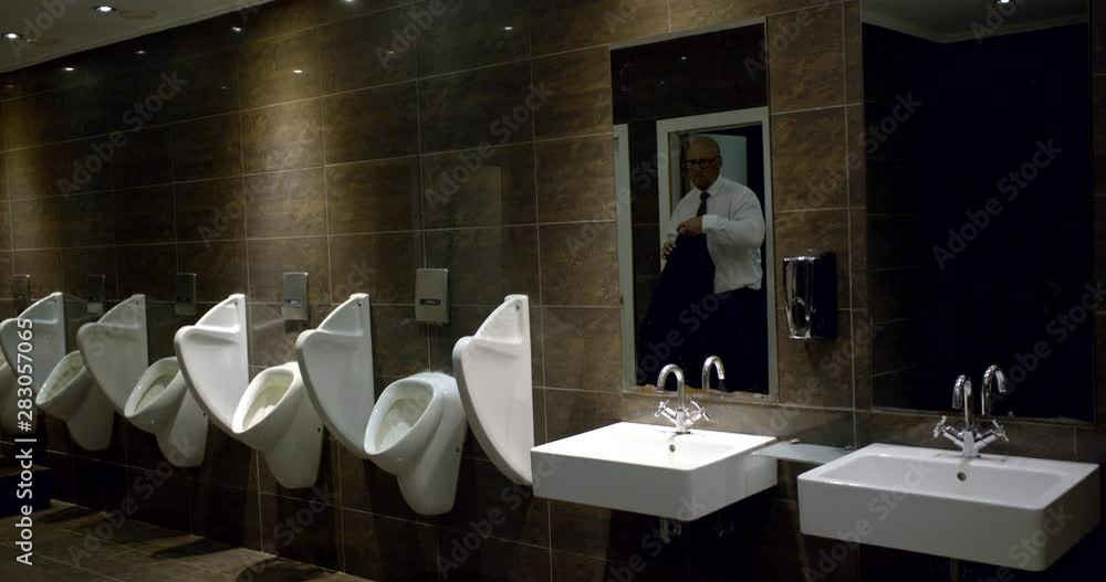 A business man comes out of the toilet cubicle into the bathroom and ...