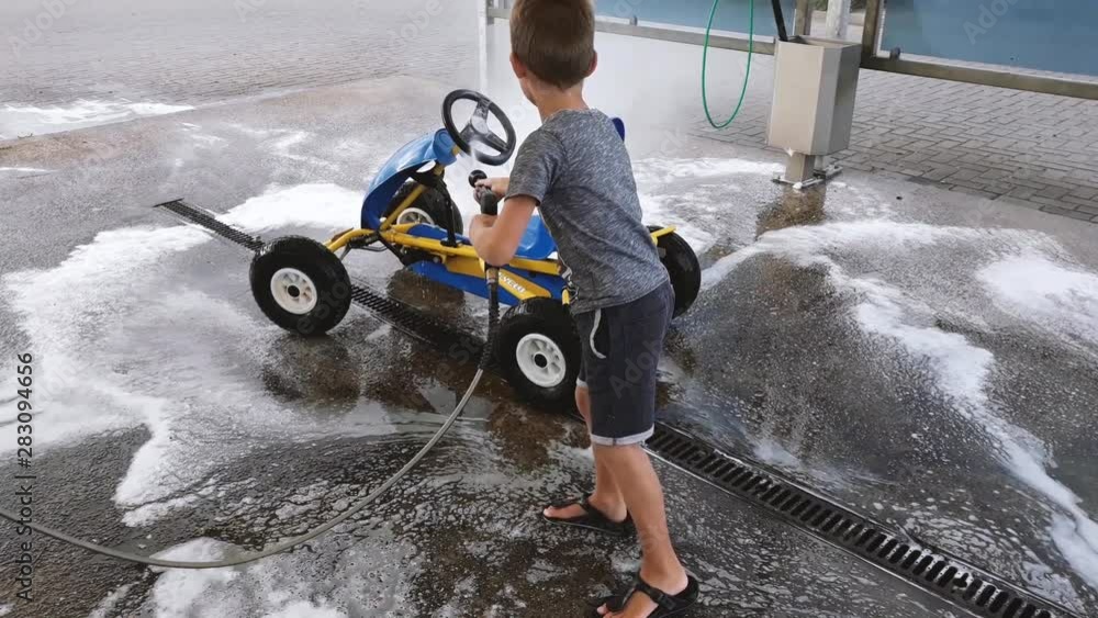 Little happy kid cleaning his yellow blue BERG-toys go-kart with an ...