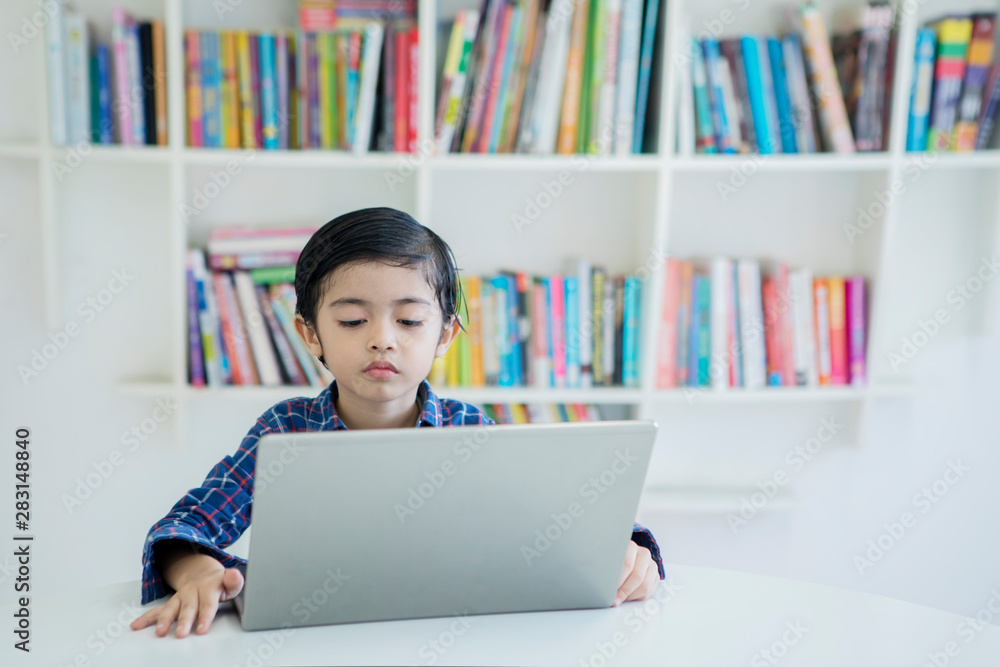 Little boy studying with a laptop in the library Stock Photo | Adobe Stock
